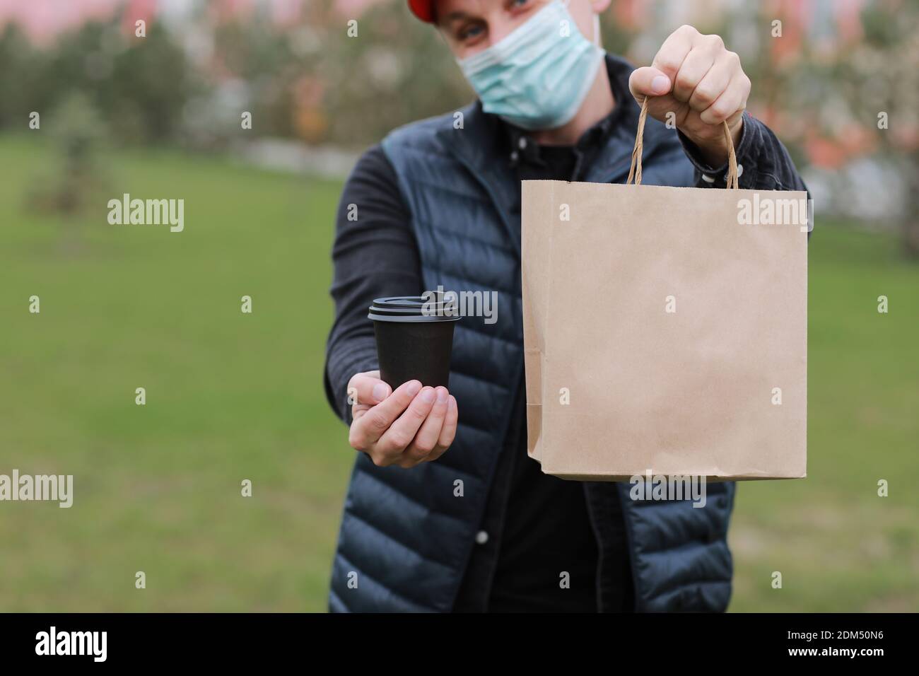 Delivery man in red cap, face medical mask hold take away paper bag and ...