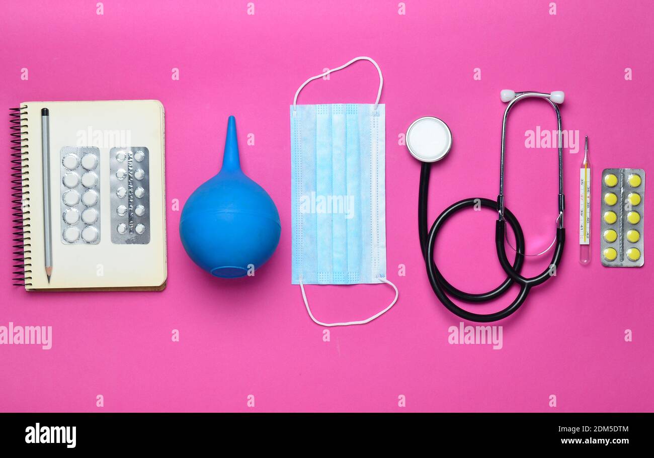 Medical equipment on a pink background. Enema, blisters pills, notepad ...