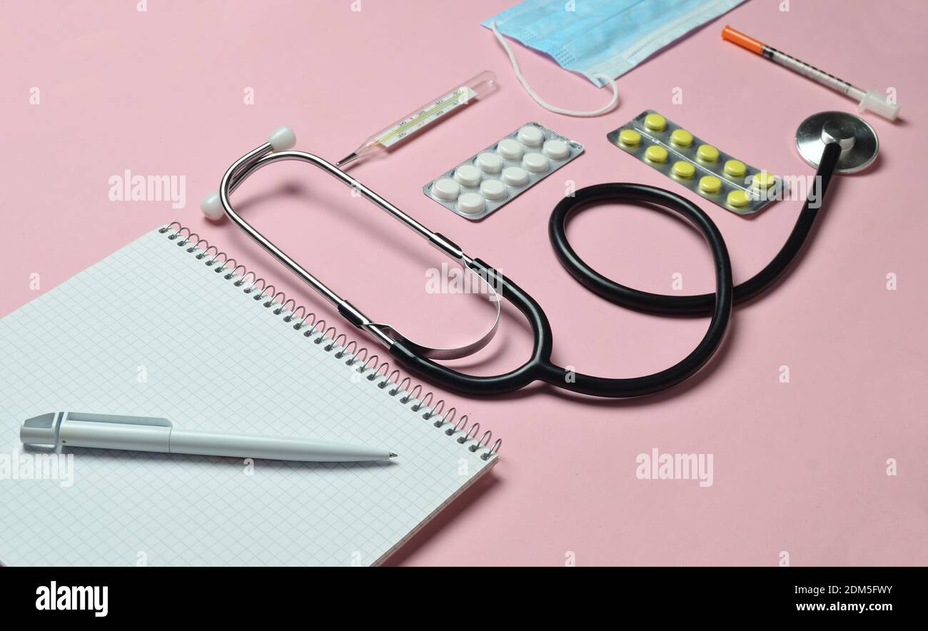 Medical equipment on a pink pastel background. Blisters pills, notepad ...