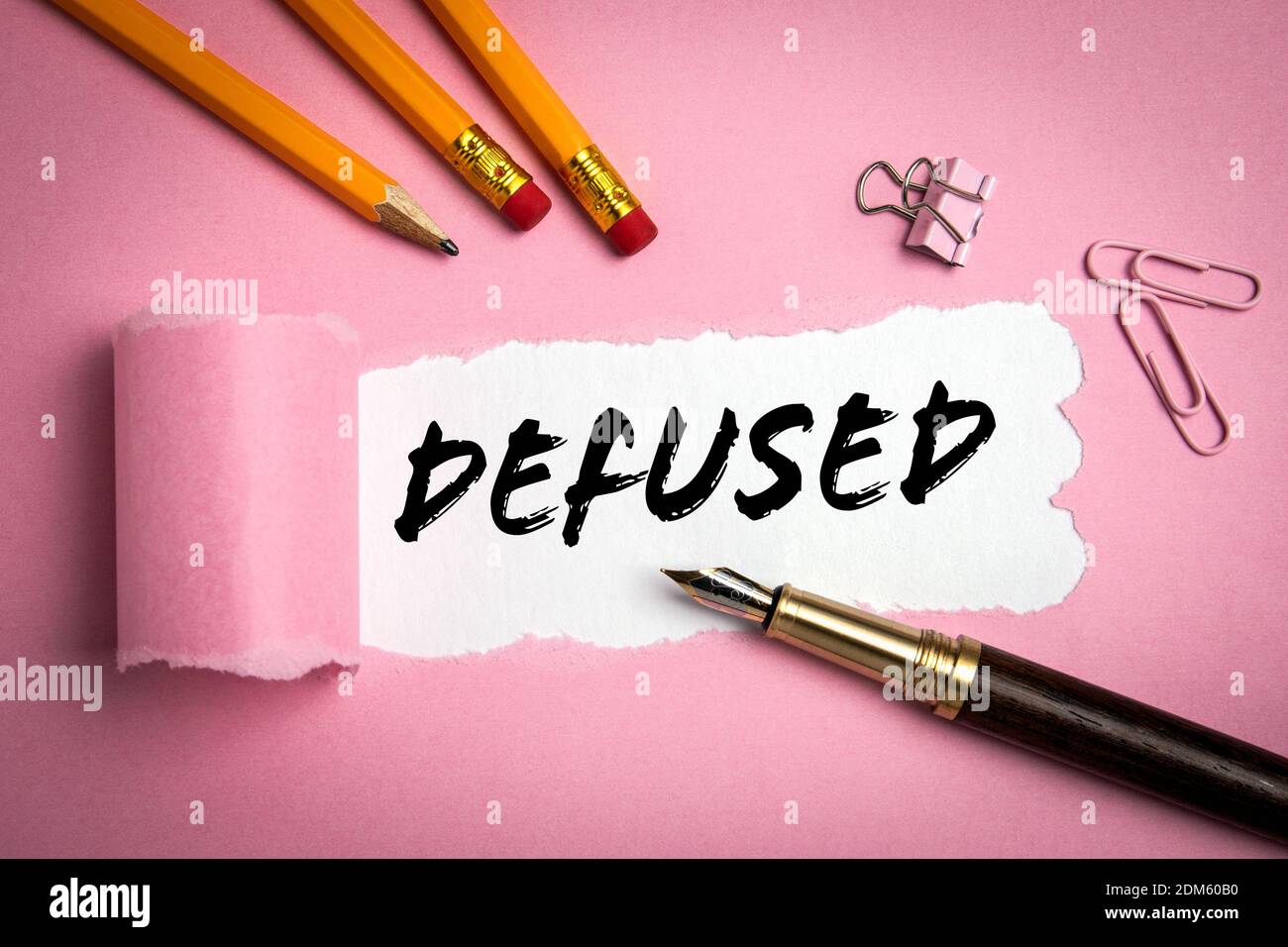 DEFUSED. Text under torn paper. Pencils and paper clips on a pink ...
