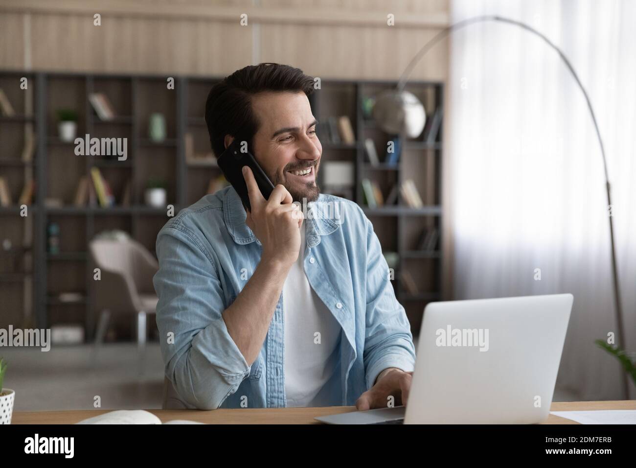 Happy man work on computer talk on smartphone Stock Photo - Alamy