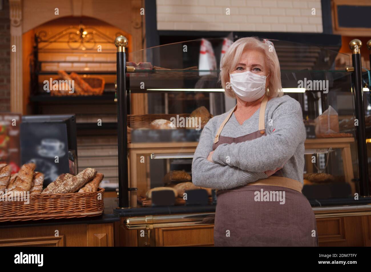 Elderly female baker wearing medical face mask, working at her bakery ...