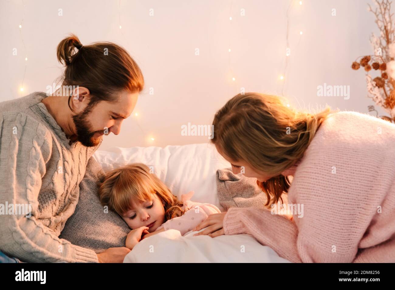 Parents kiss and caress their daughter who sleep in bed Stock Photo - Alamy