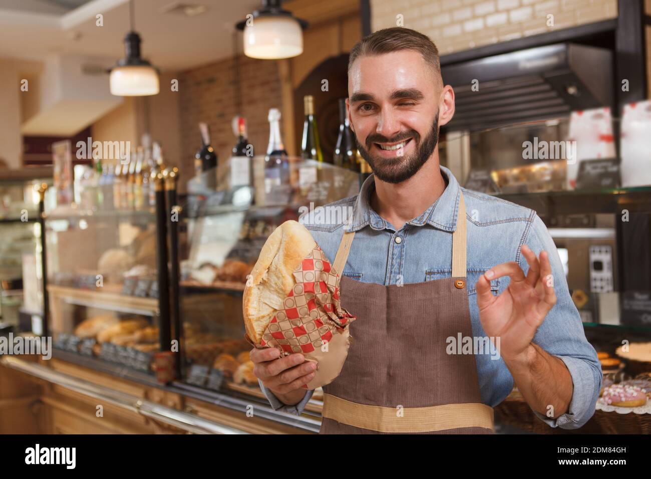 Cheerful male baker smiling, showing ok sign while selling delicious ...