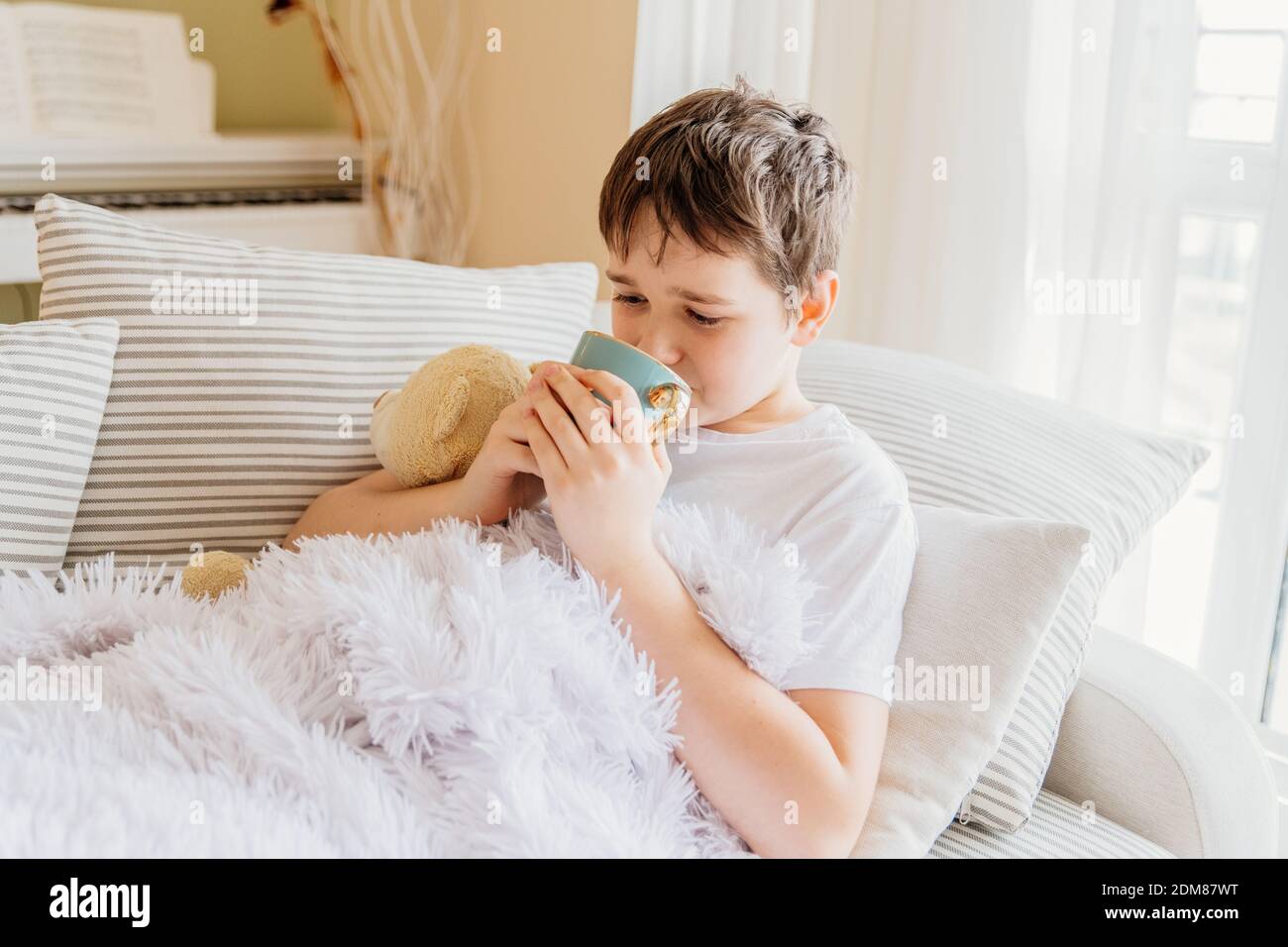 The sick boy lies under the blanket and drinks the medicine Stock Photo ...
