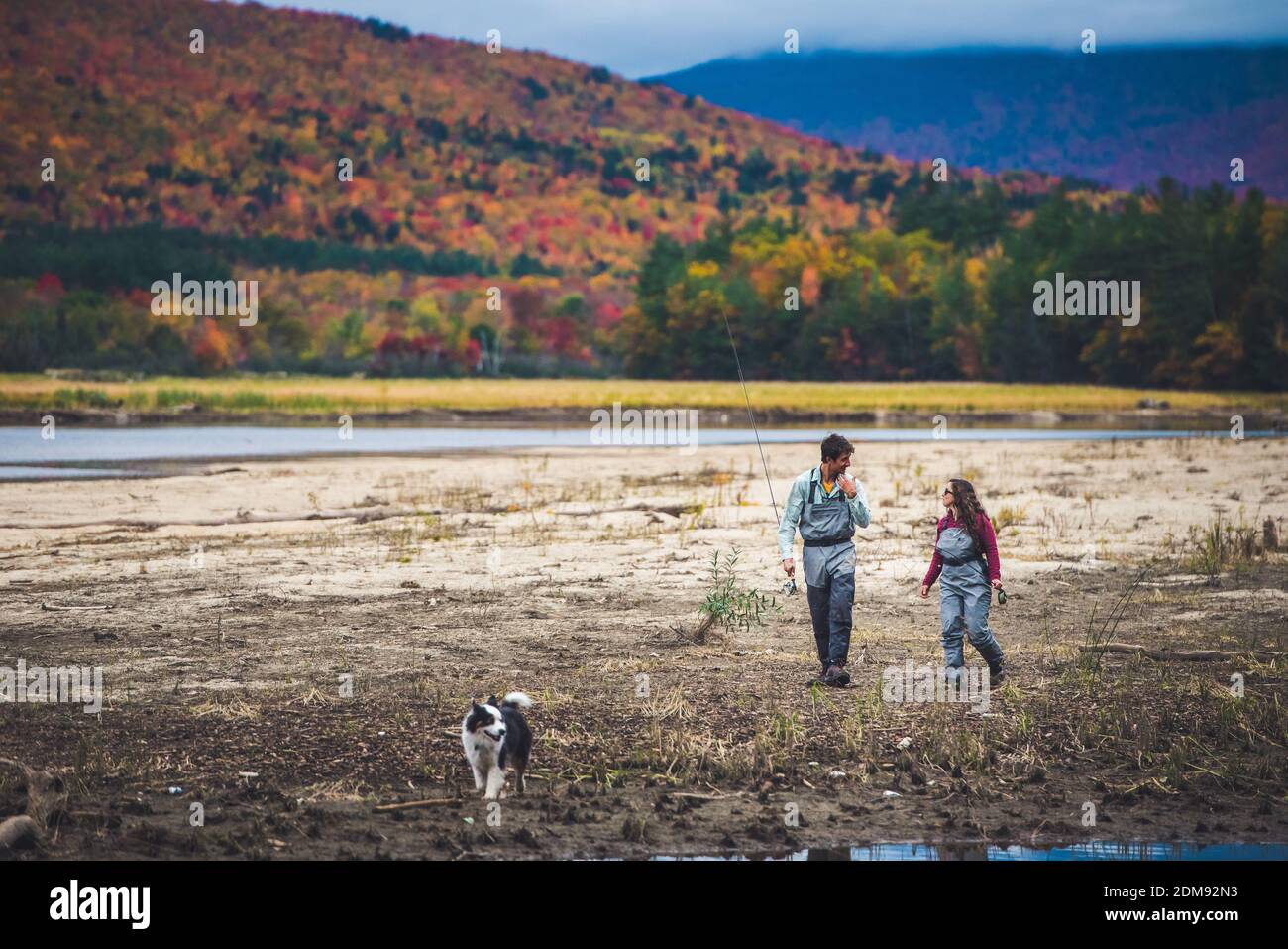 Male and female anglers walk down the shore with dog and foliage Stock ...