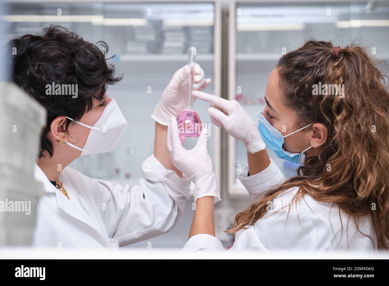Two young female scientists wearing face masks using a flask ...