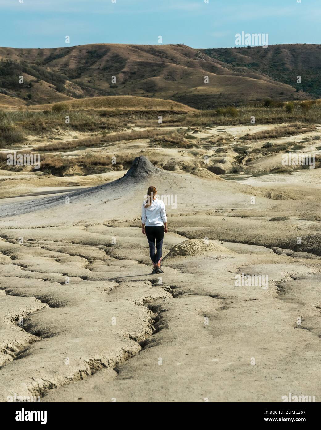 Young girl facing a mud volcano standing on cracked dry soil, Romania ...