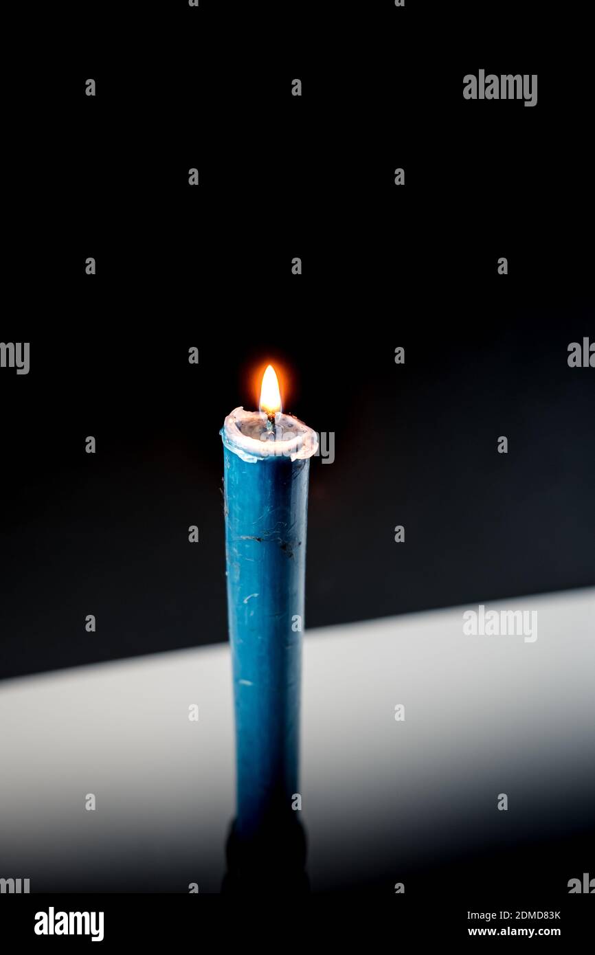 A vertical closeup shot of a single long candle with a burning flame ...