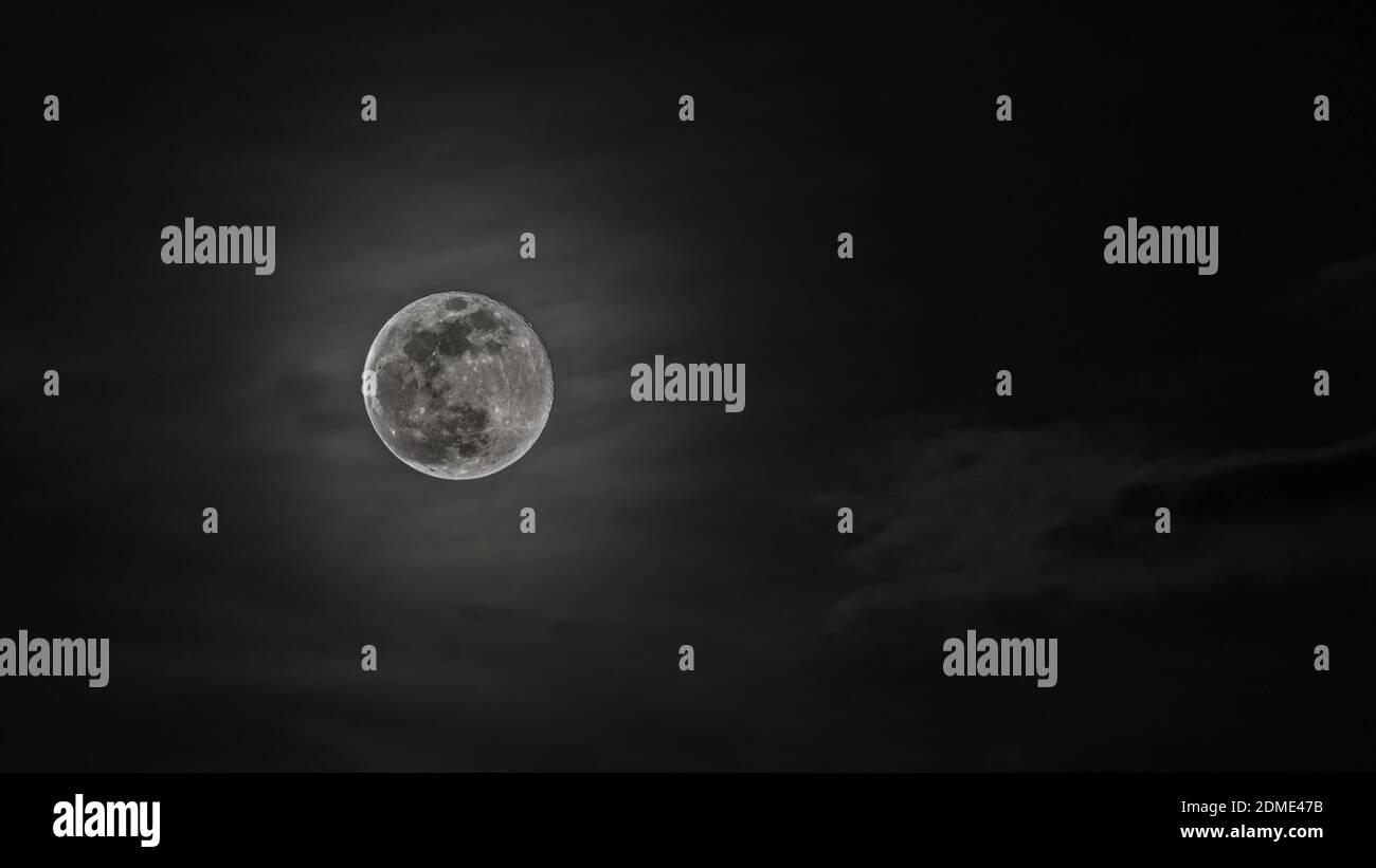 A grayscale shot of the shiny full moon on a cloudy sky at night ...