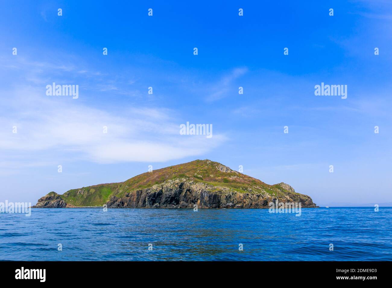 A small uninhabited green island in the middle of a calm blue sea and ...