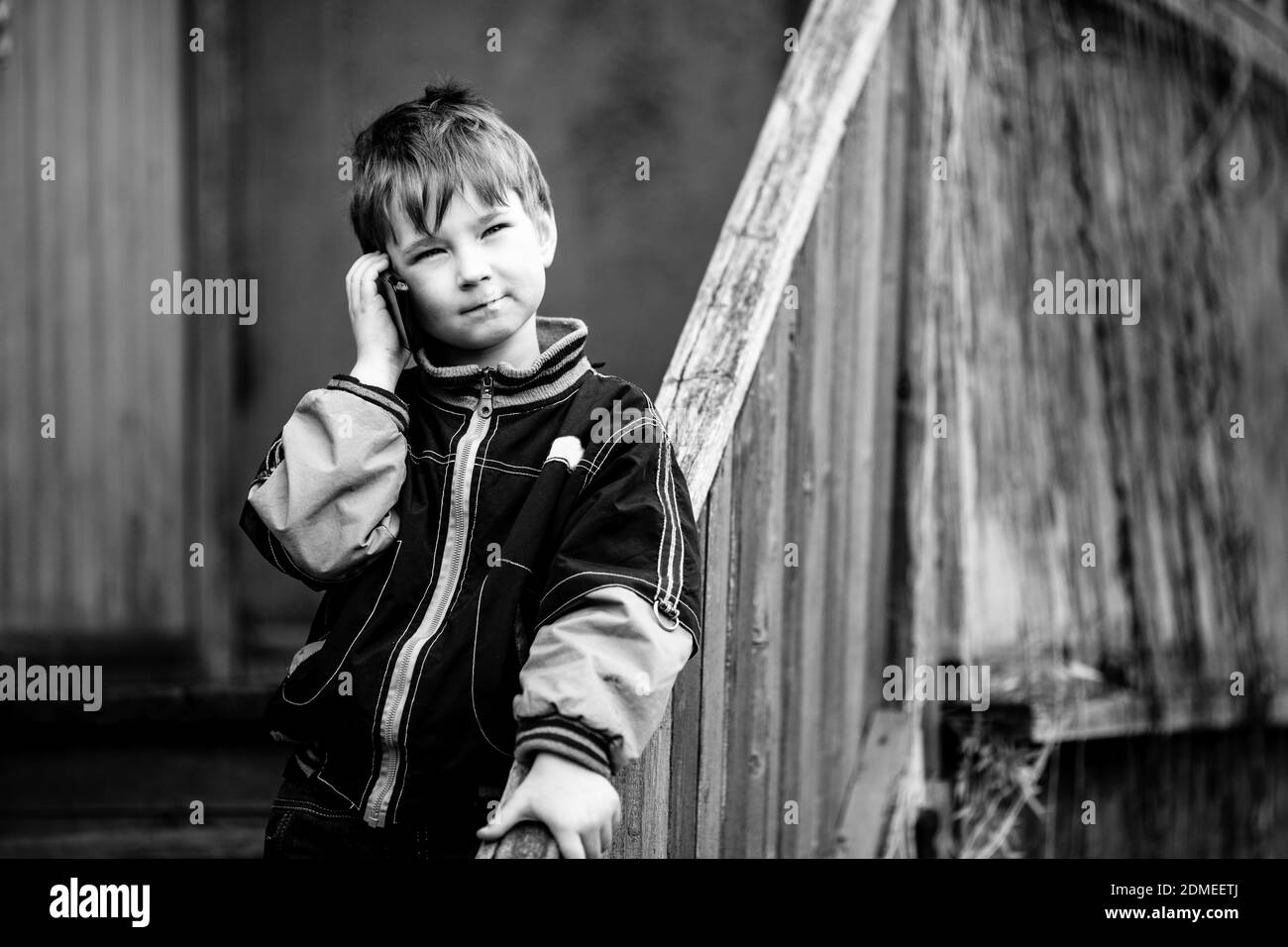 Little boy calls on the phone while standing outdoors. Black and white ...