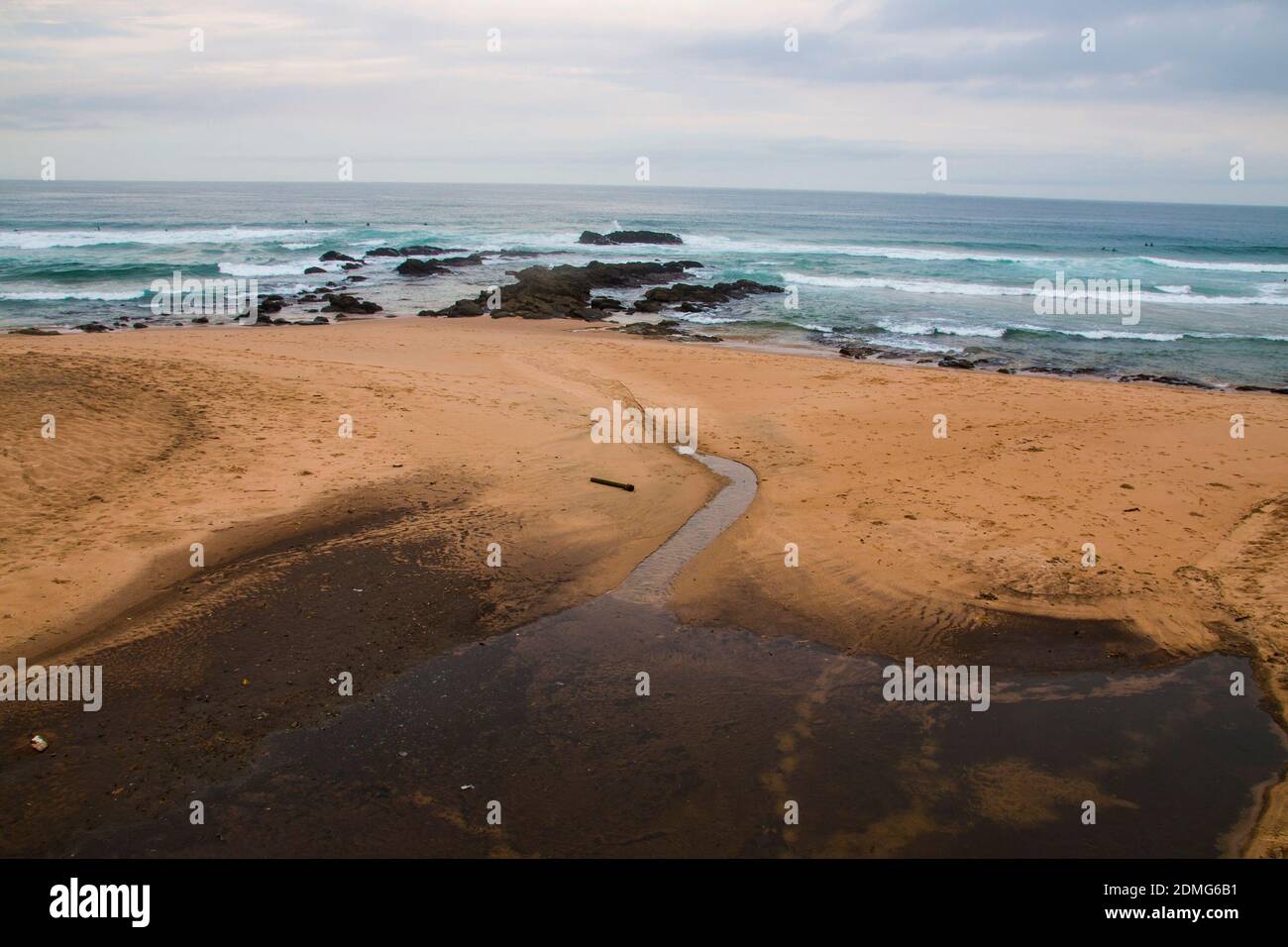 Stream running onto beach with waves and rocks in background Stock ...