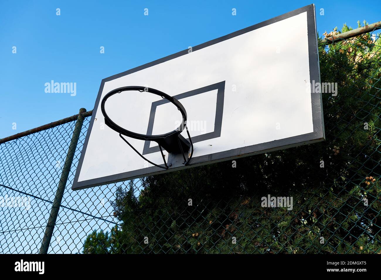 Outdoor basketball hoop in a court mounted on a fence wire against blue ...