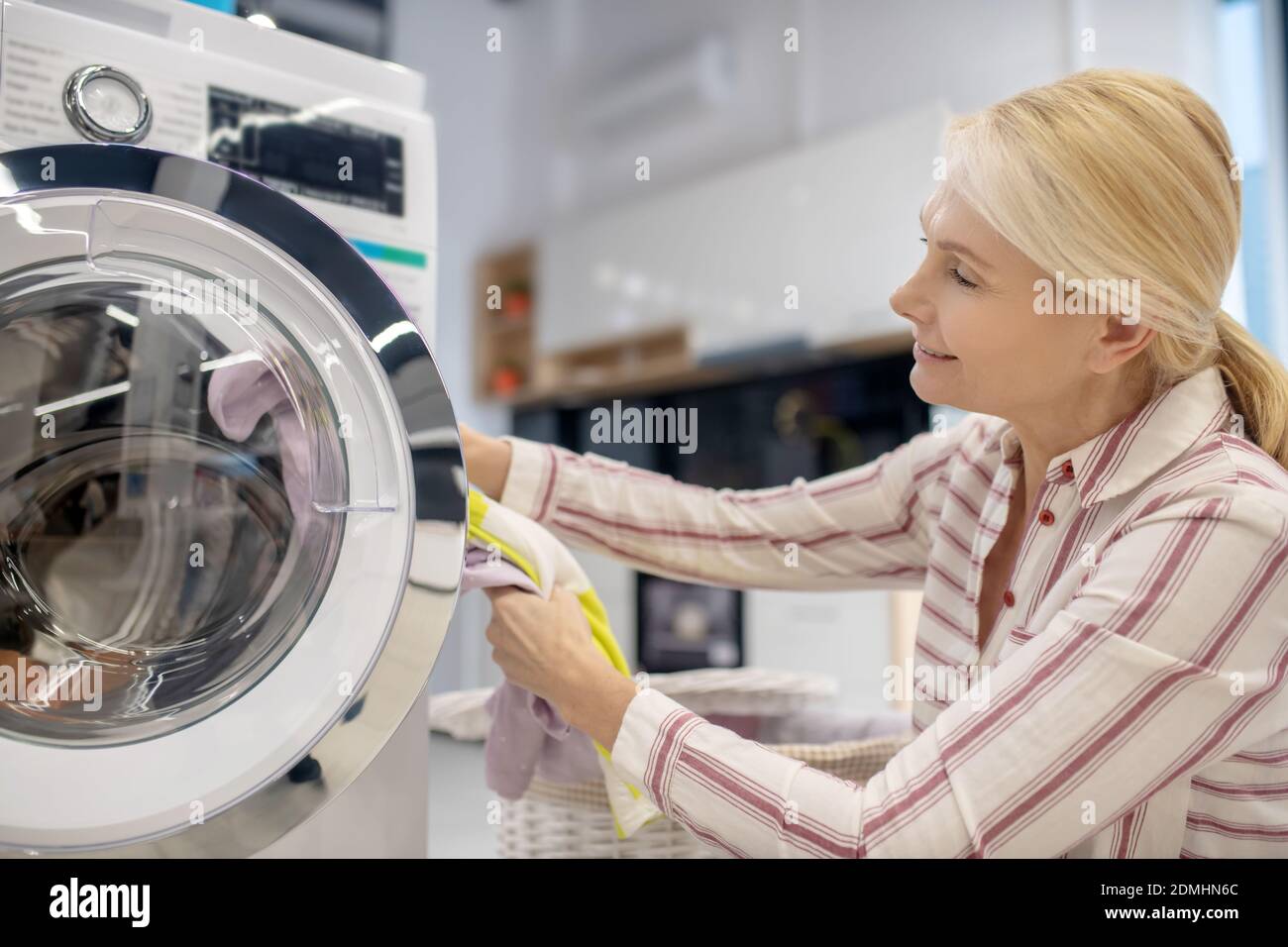 Blonde housewife putting clothes into washing machine Stock Photo - Alamy