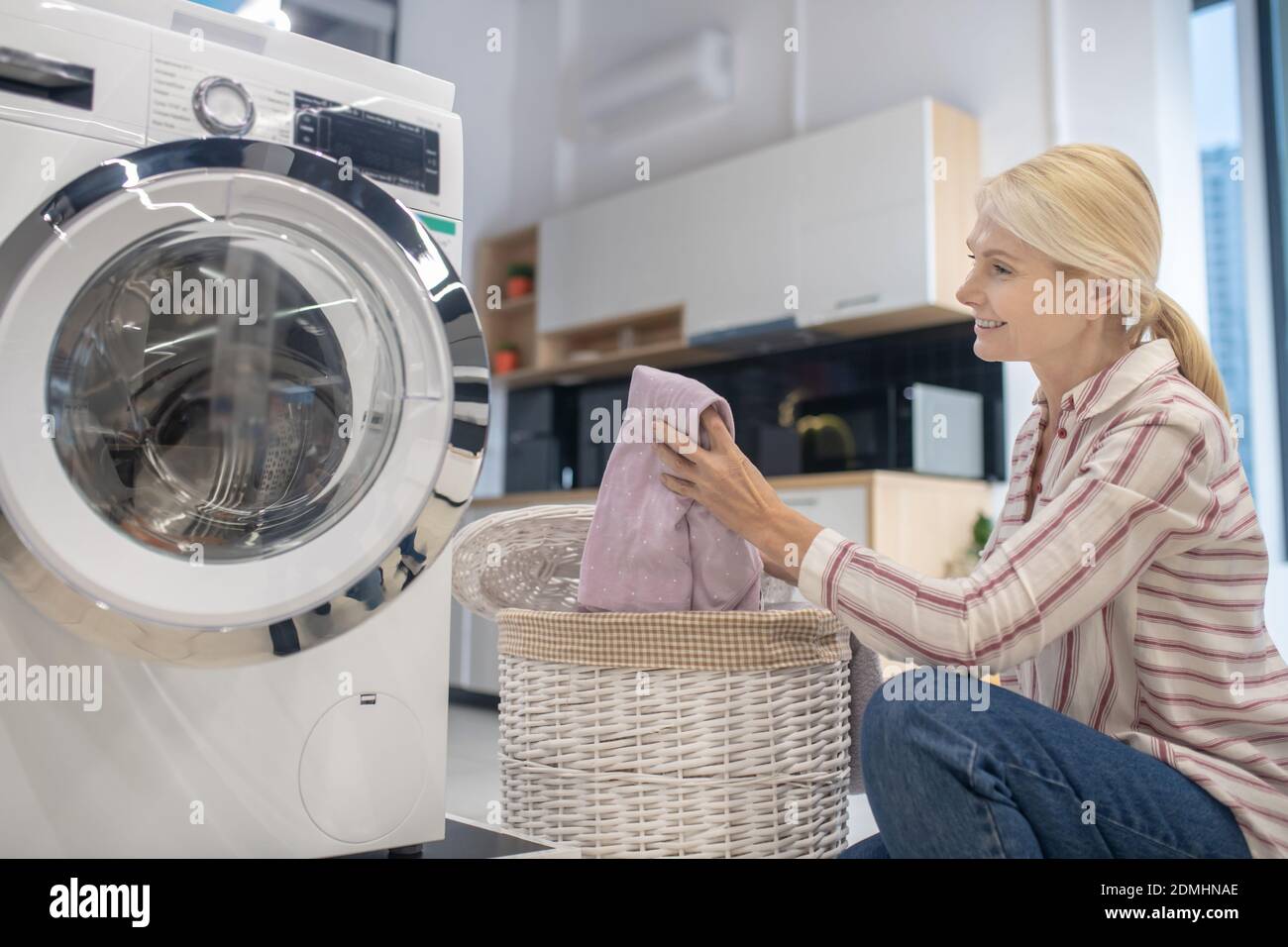 Blonde housewife putting clothes into washing machine Stock Photo - Alamy