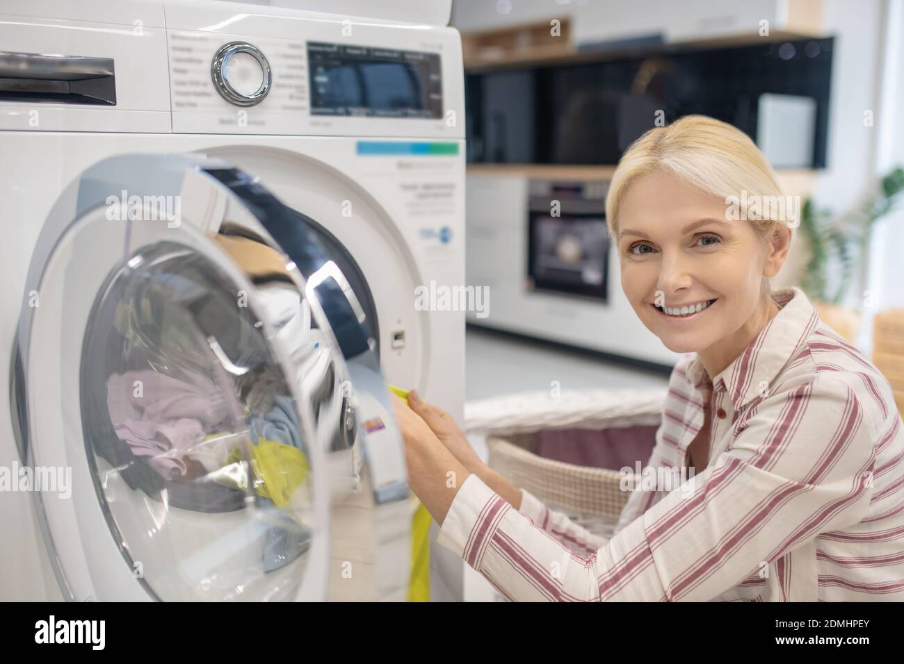 Blonde woman putting clothes into washing machine and smiling Stock ...