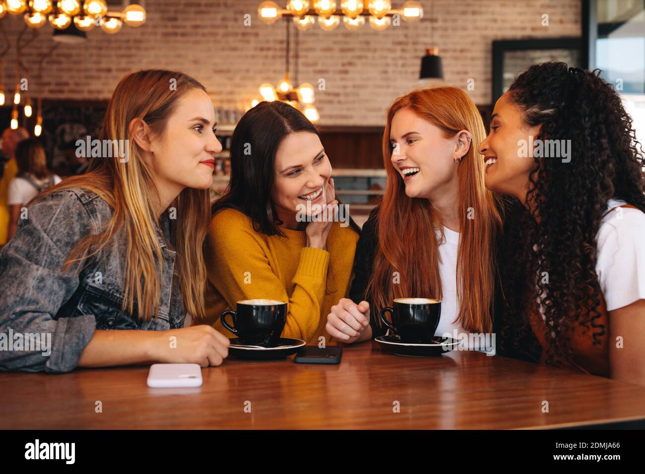 Happy young people sitting together at a cafe having gossip over cup of ...