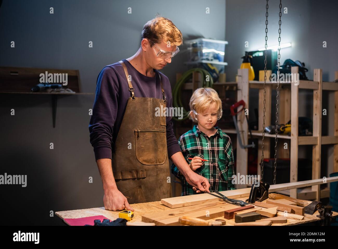 a young male carpenter is teaching woodwork to a young boy in his ...
