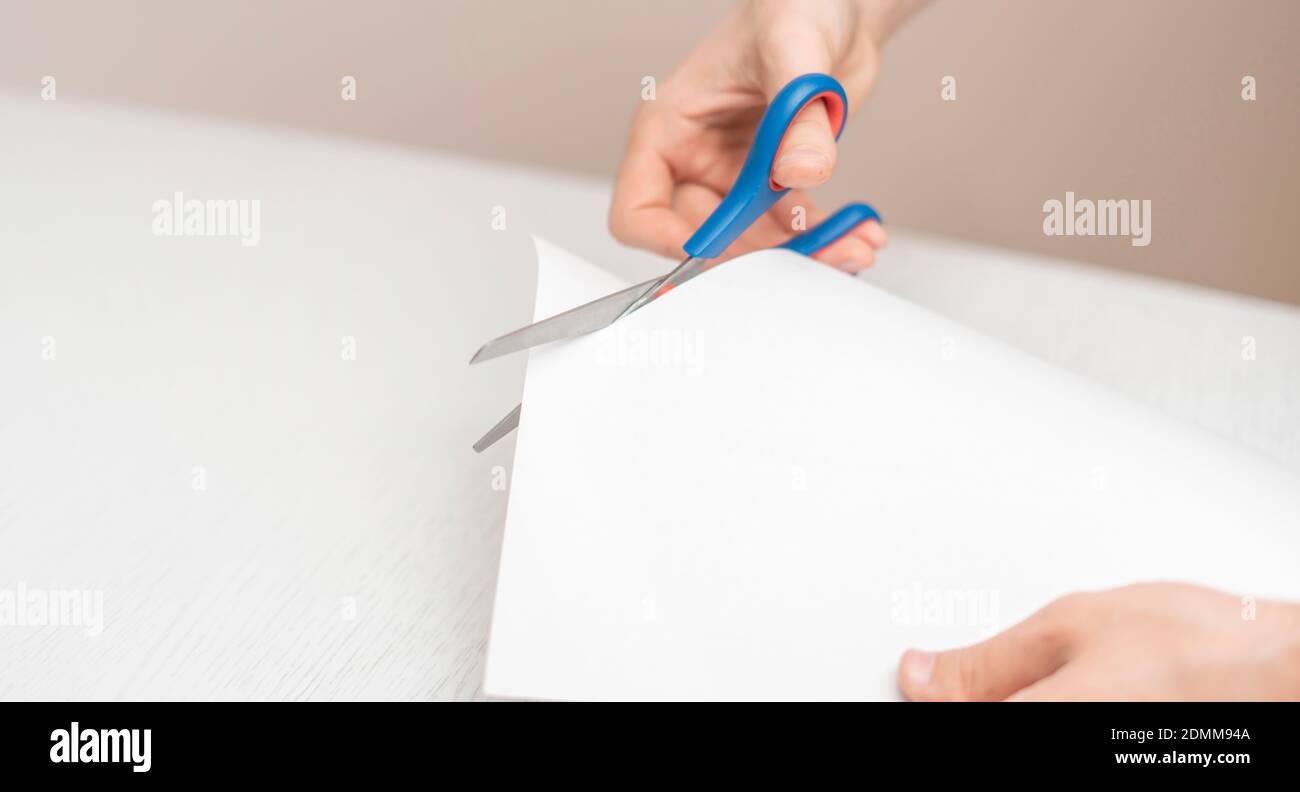 person's hands holding piece of paper sheet and cut it with scissors ...