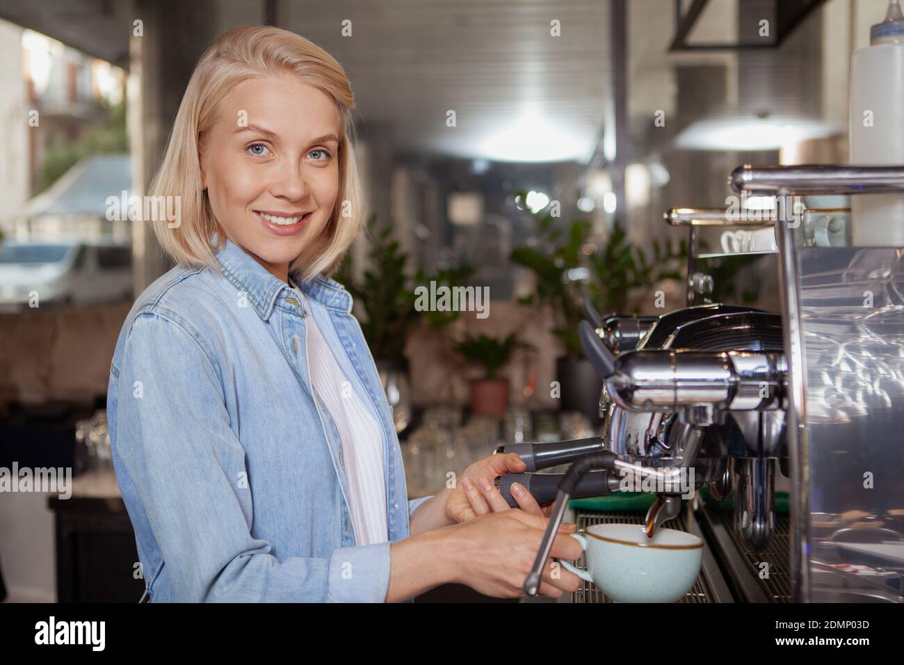 Cheerful beautiful female barista smiling to the camera while preparing ...