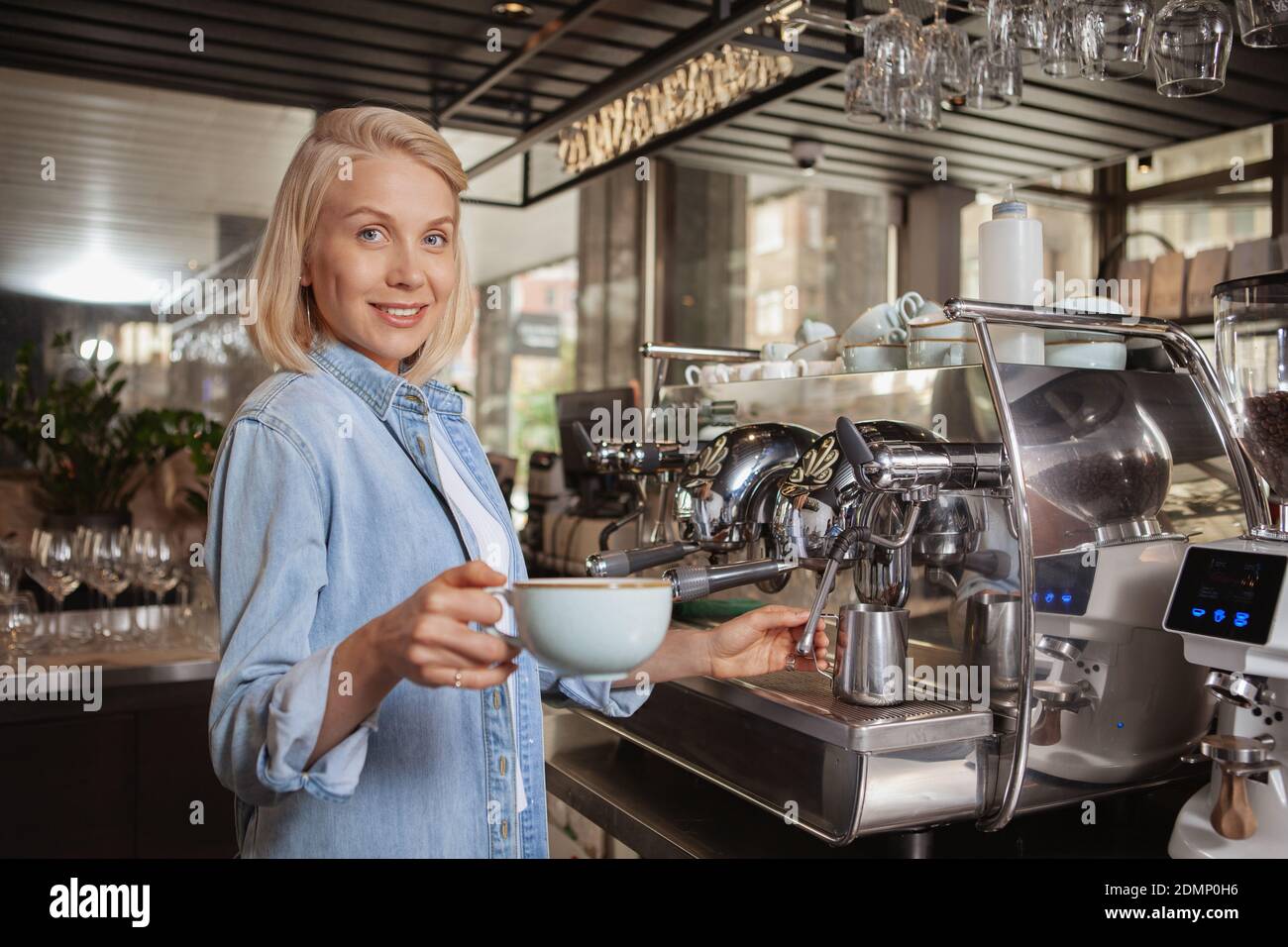Lovely blond haired female barista smiling, holding out a cup of ...