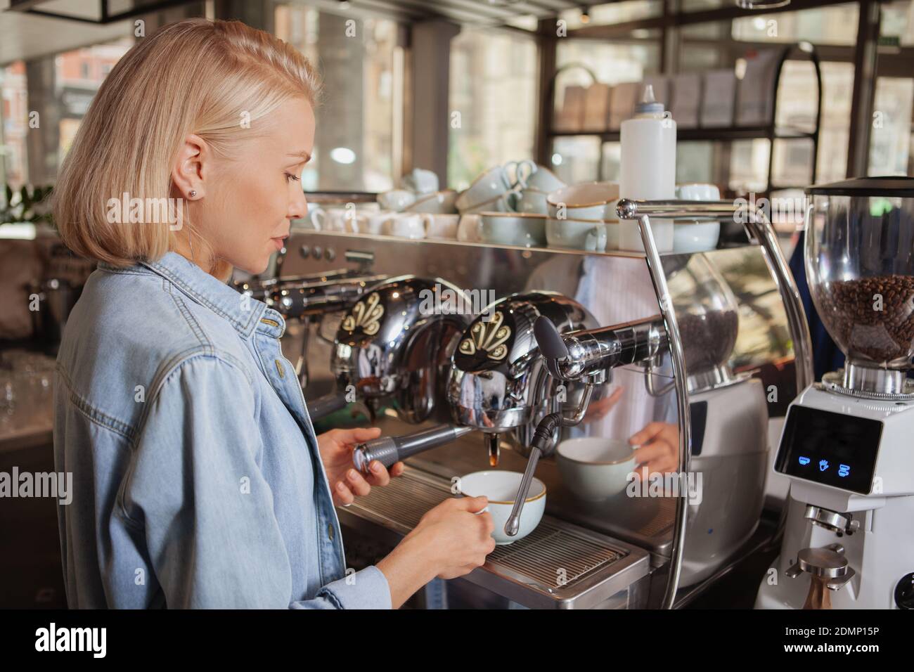 Rear view shot of a blond haired female barista using coffee machine ...