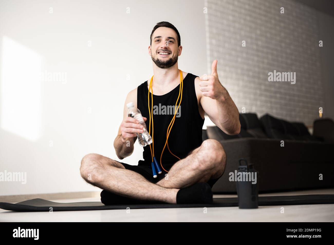Young man exercising at home. Guy sits alone on black yoga map, holds ...