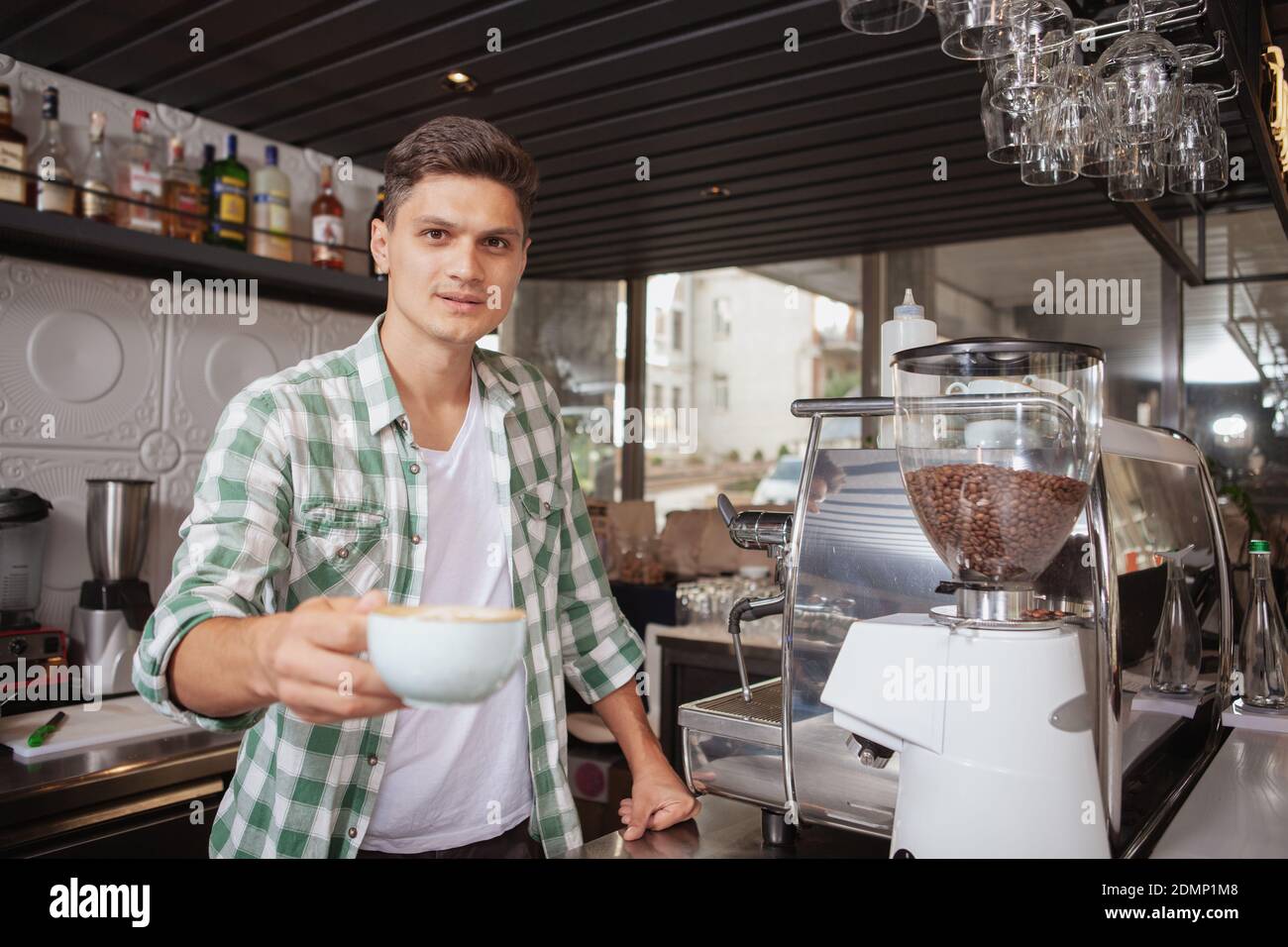 Charming male barista smiling, holding out a cup of delicious hot ...