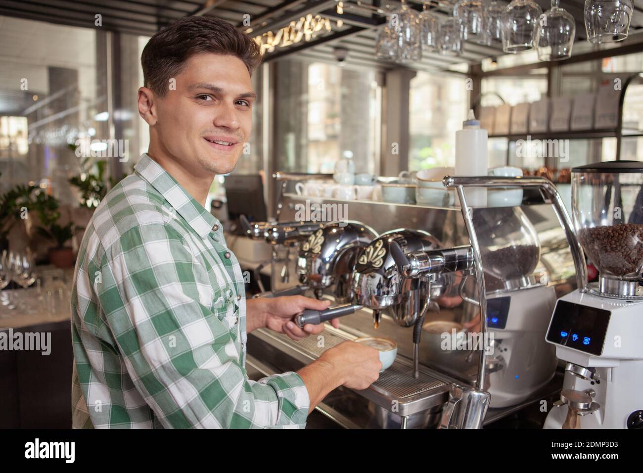 Attractive male barista smiling to the camera over his shoulder, using ...