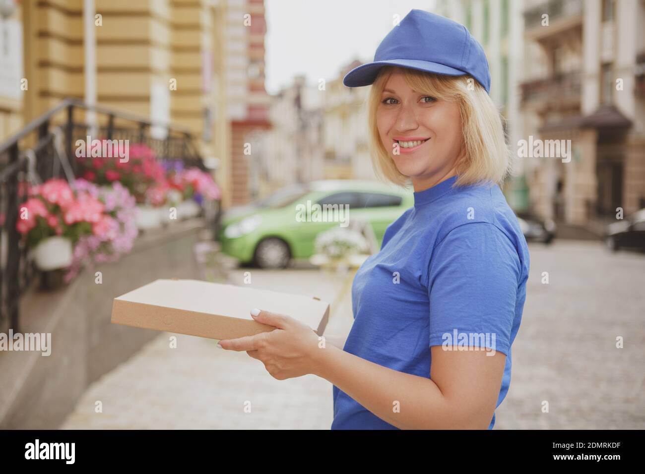 Charming young female courier delivering pizza in the city, copy space ...