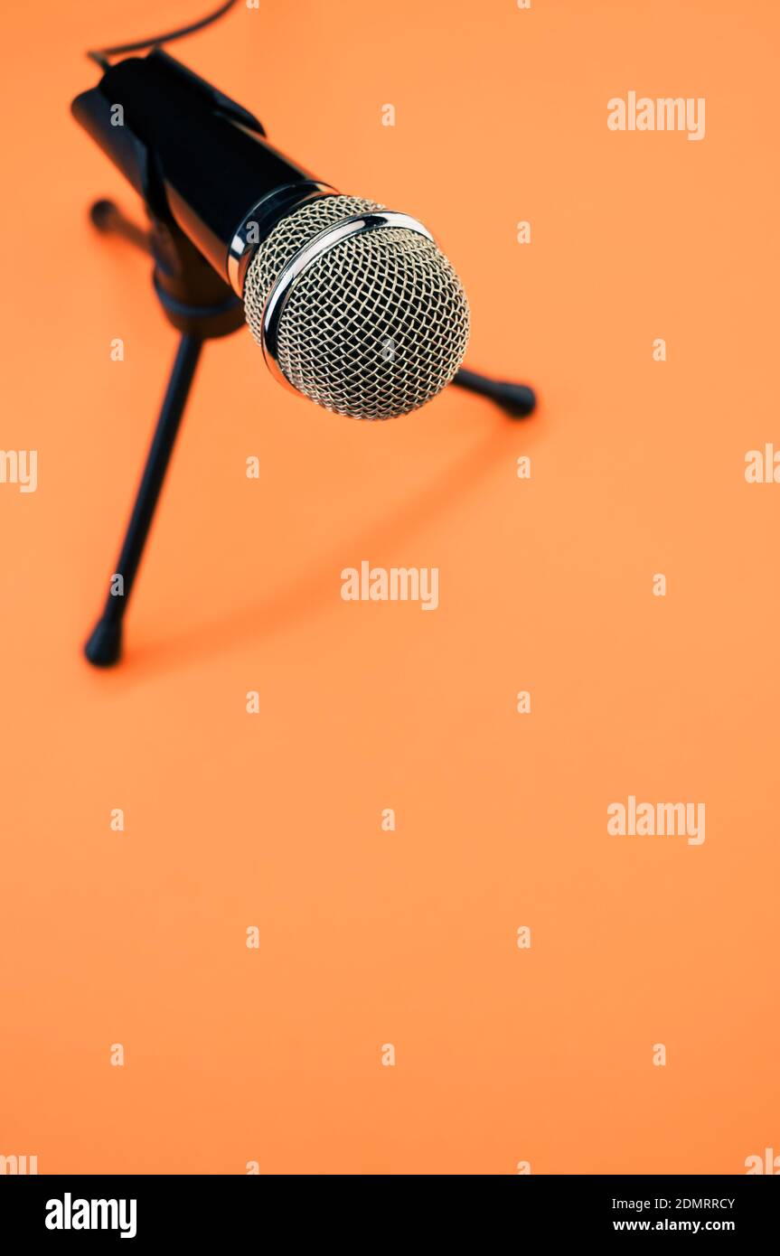 A vertical shot of a microphone on a small stand, on an orange surface ...