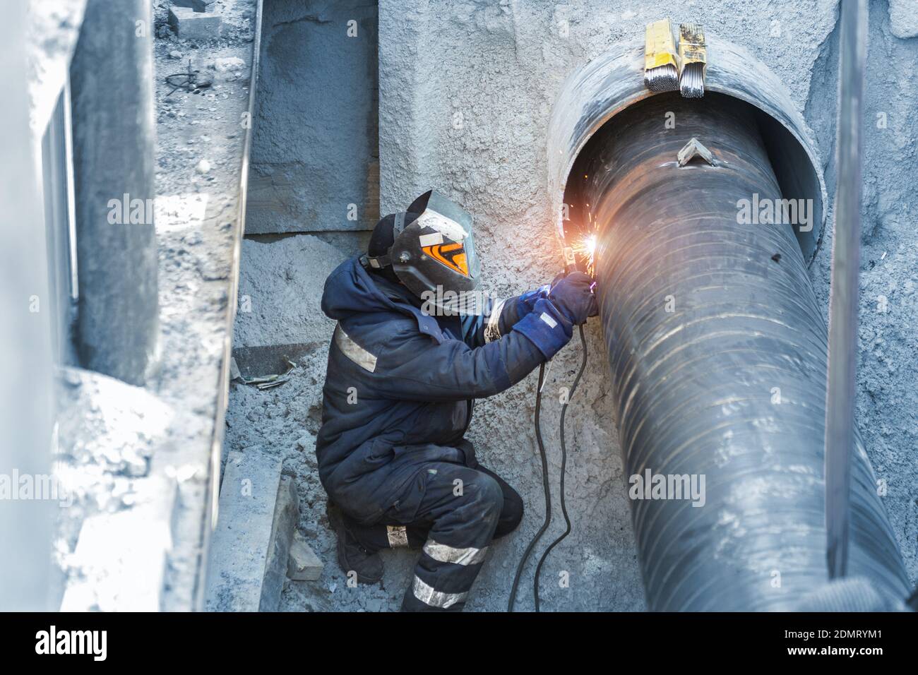 Professional welder welding water or gas steel pipeline in protective trench and mask at ...