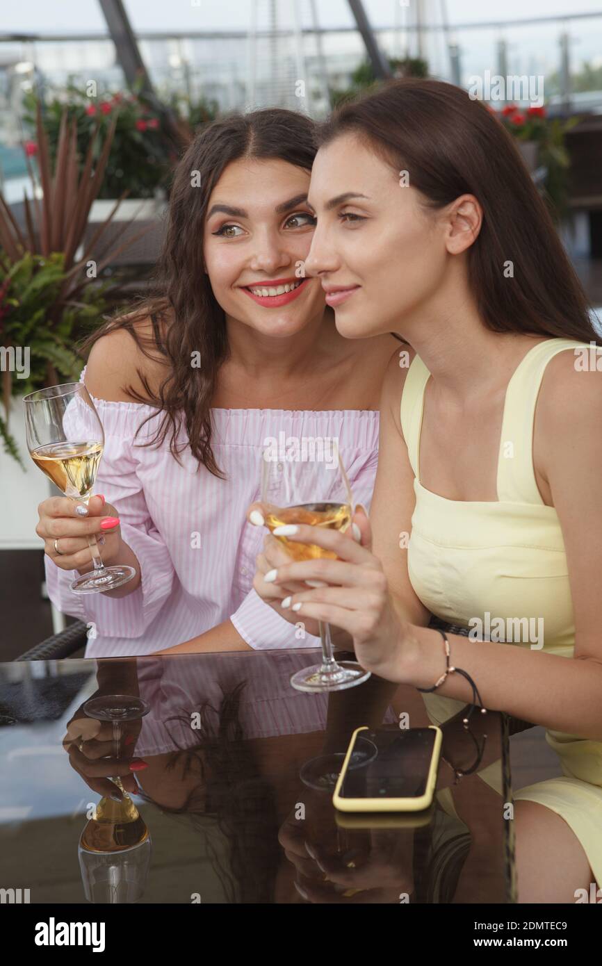 Vertical shot of two lovely young women gossiping over drinks at ...