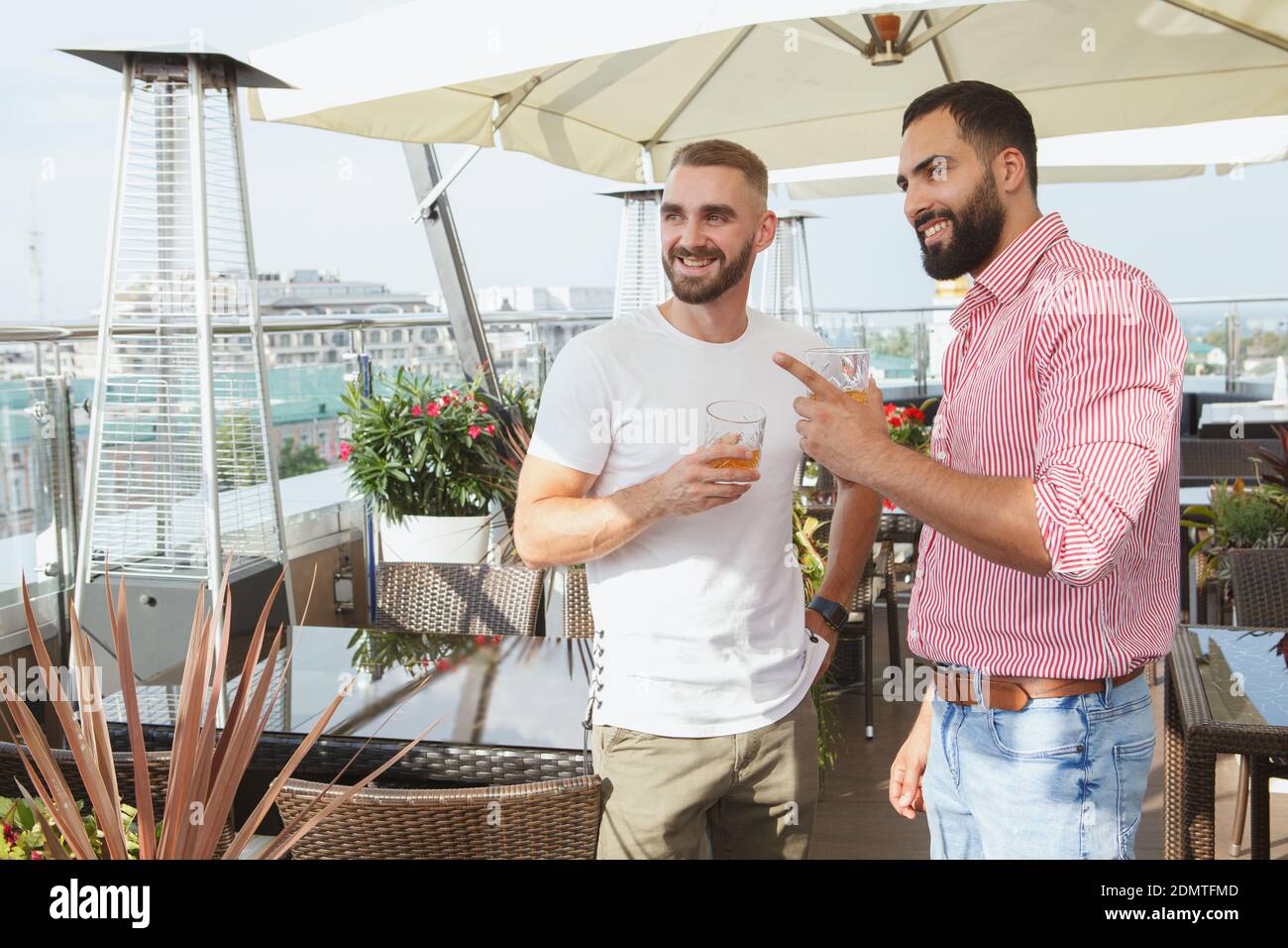 Two handsome stylish men talking over drinks at modern rooftop ...