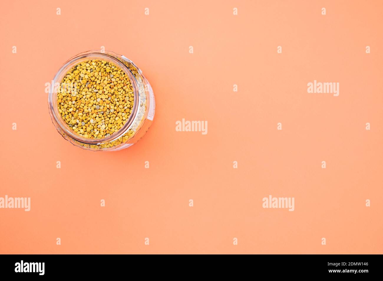 A top view of organic bee pollen in a glass jar, on an orange surface ...