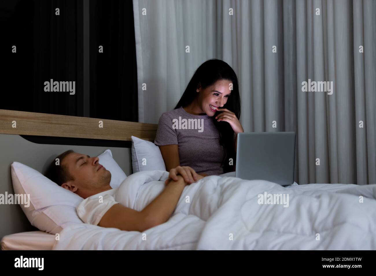 Woman sitting on bed in the night and using laptop computer while ...