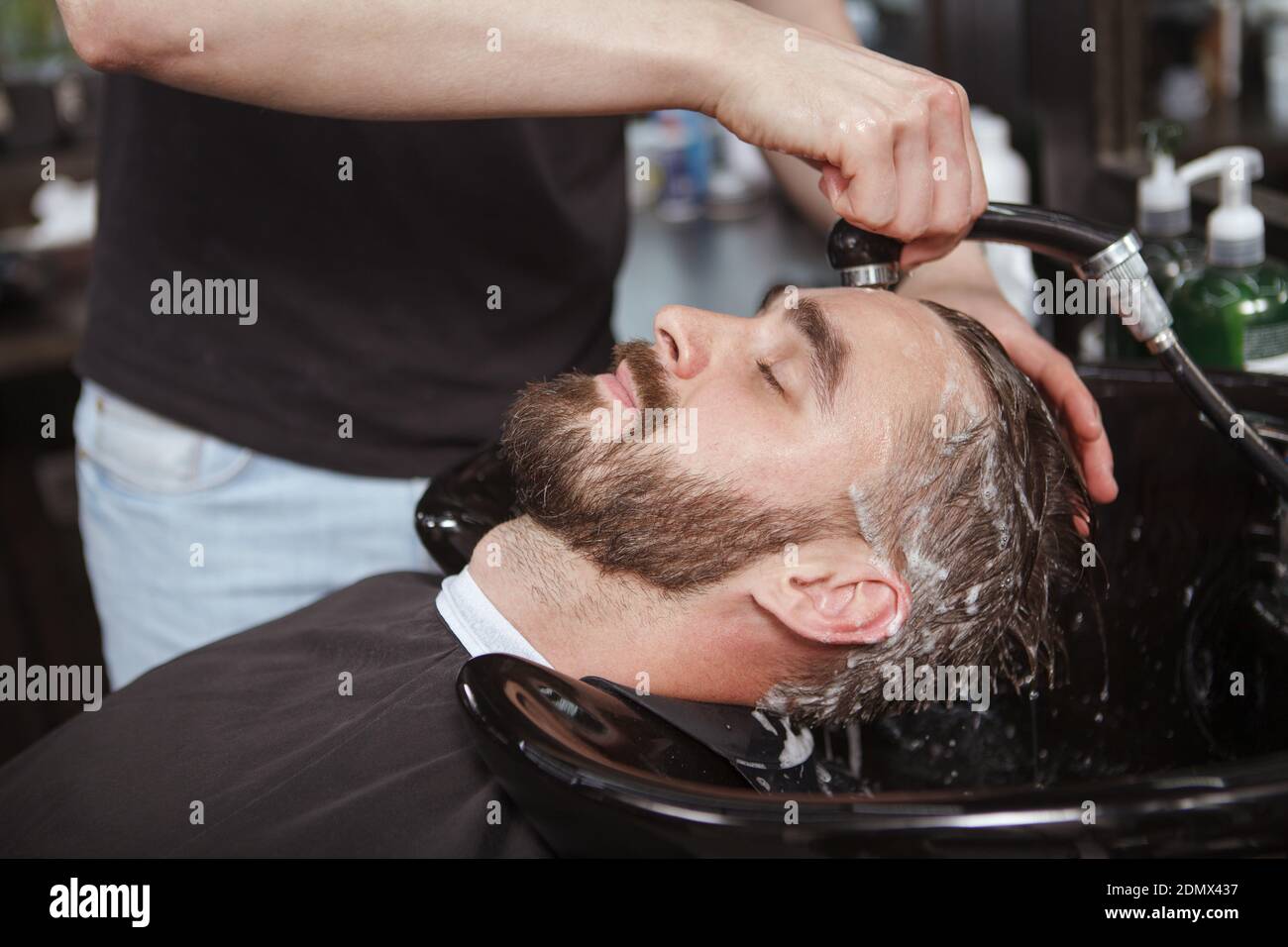 Bearded man enjoying hair wash by professional barber at the salon ...