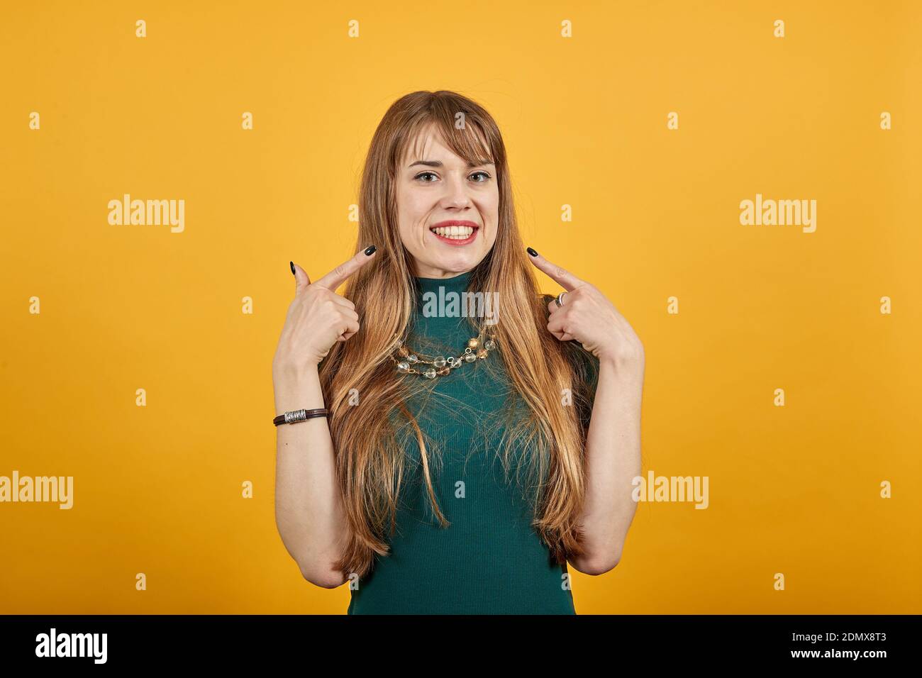 Pointing fingers at cheeks. Cheerful posing with finger on cheek ...