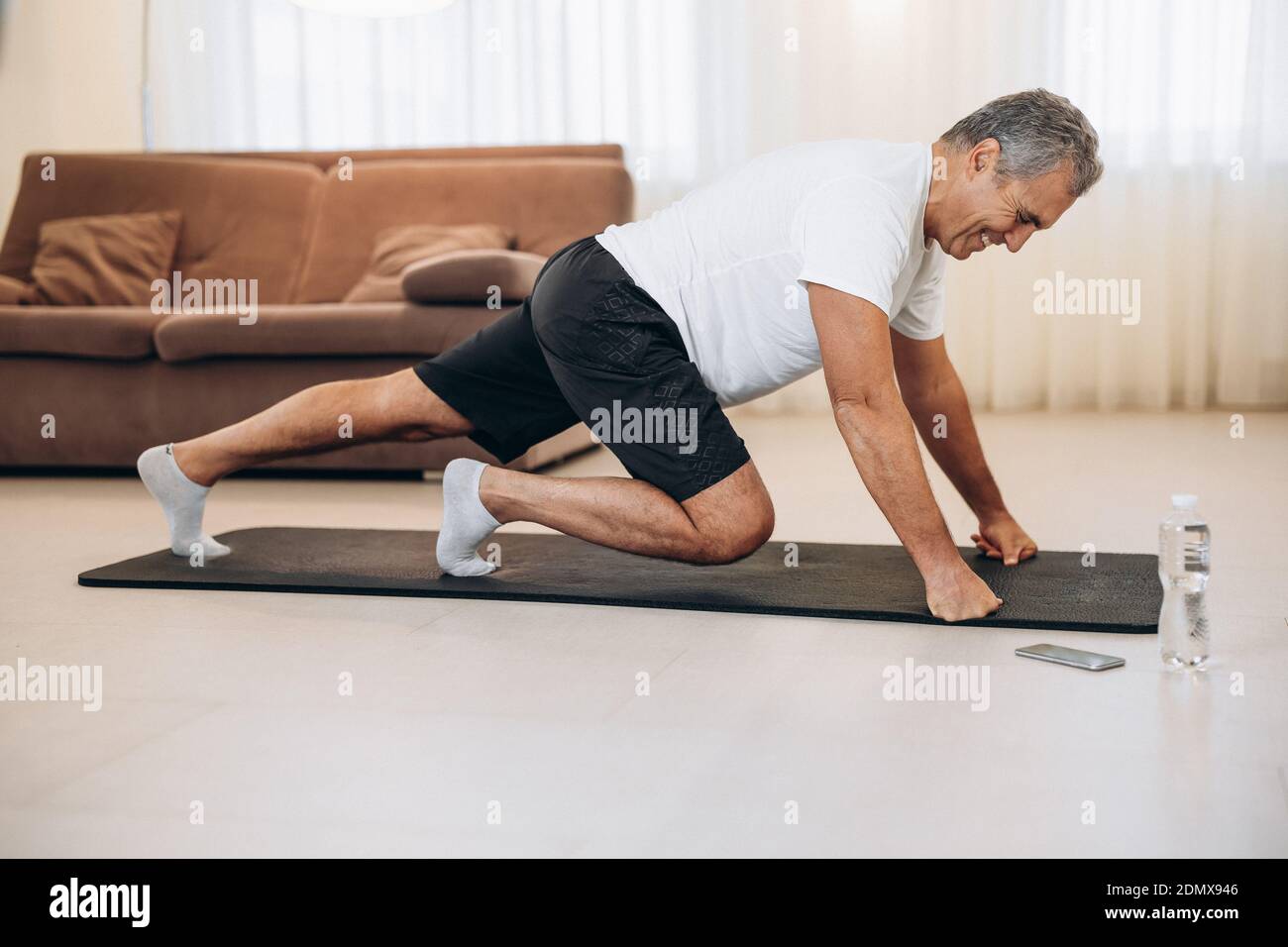 Elderly man doing mountain climber exercises on black yoga mat. Morning ...