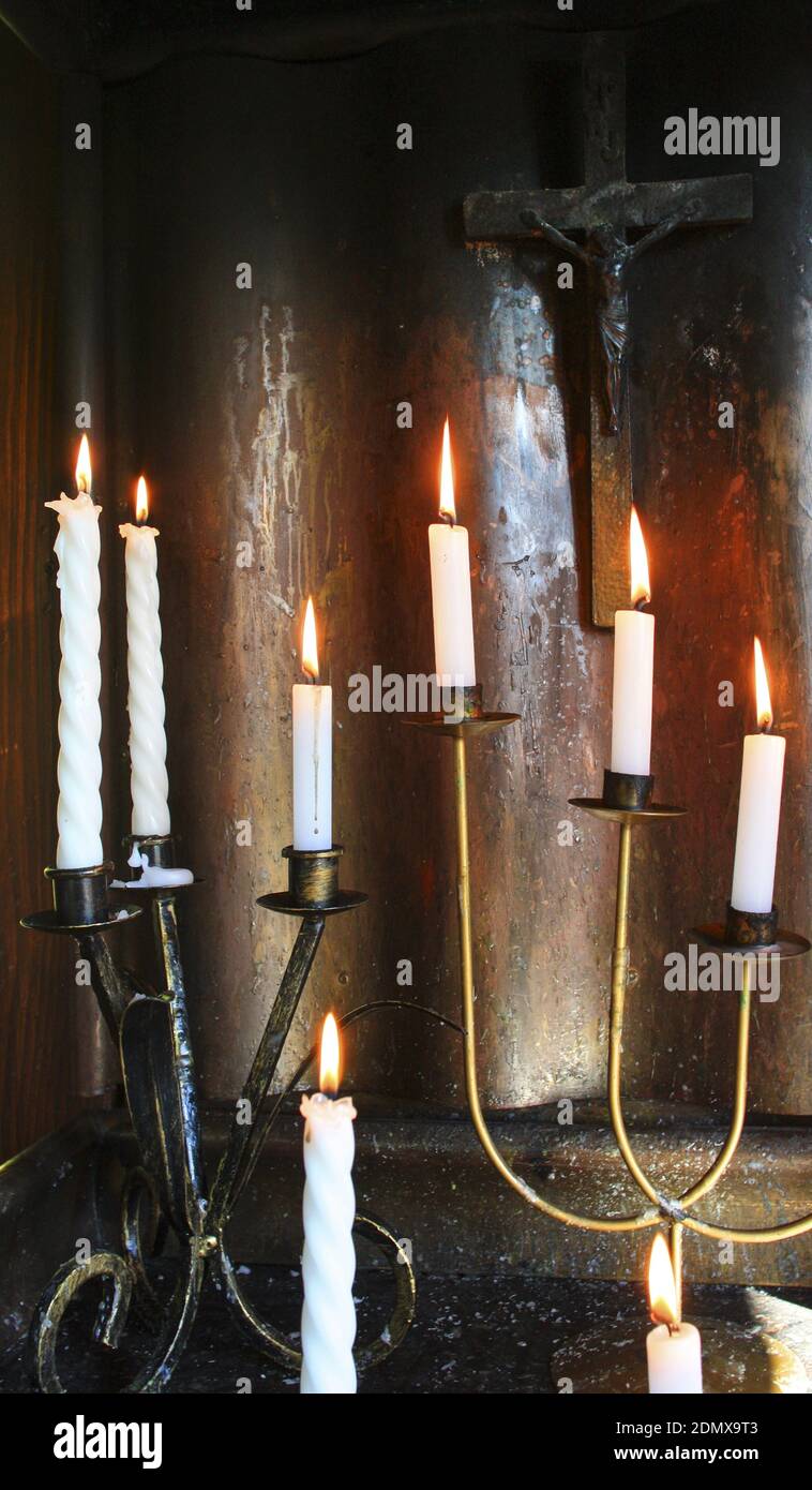 White candles burns in old shrine. Cross with Jesus in the background ...