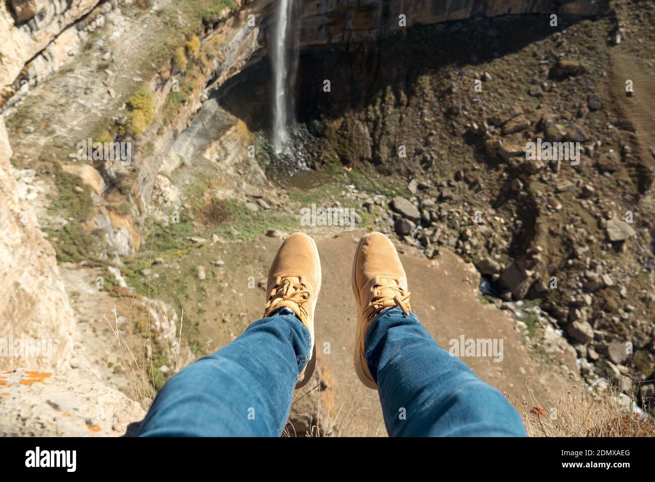 Person in blue jeans and beige sneakers sits swinging legs on high ...