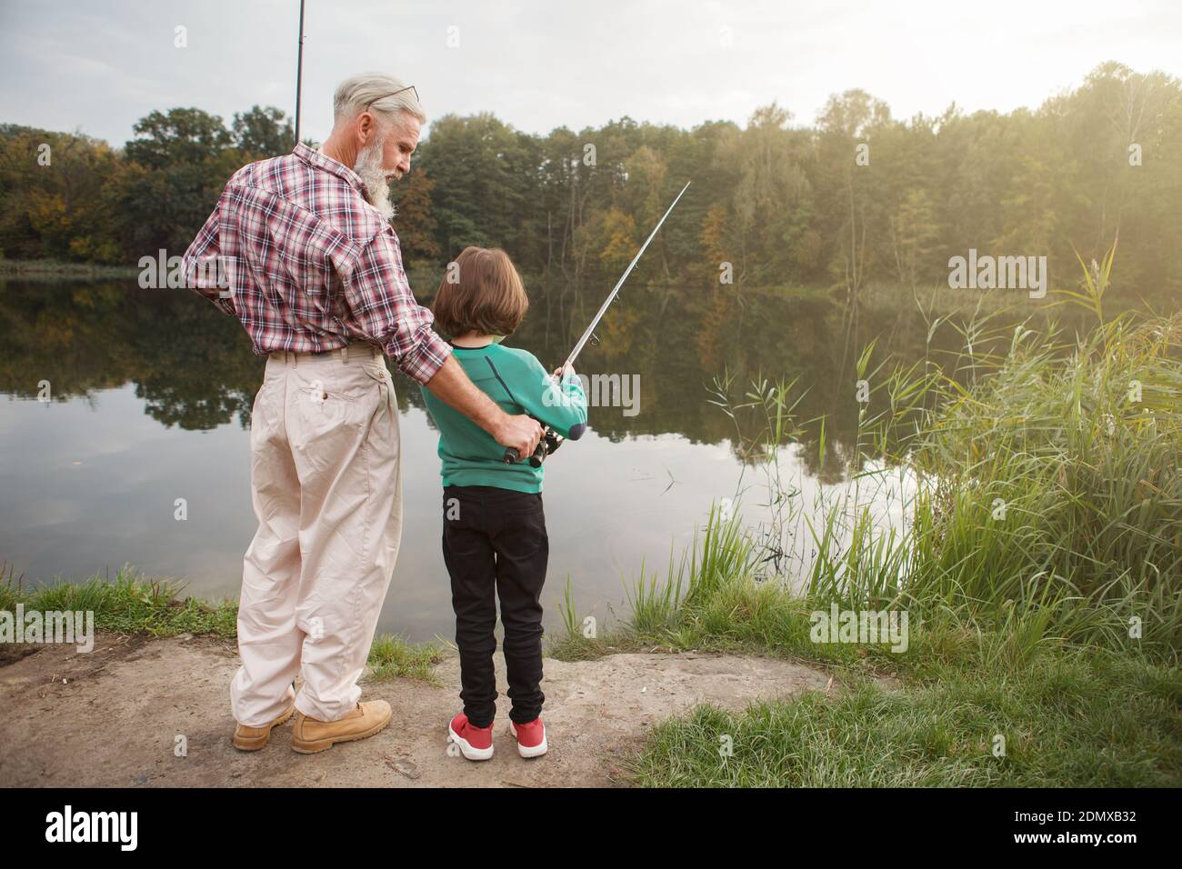 Rear view shot of a little boy learning fishing with the help and ...