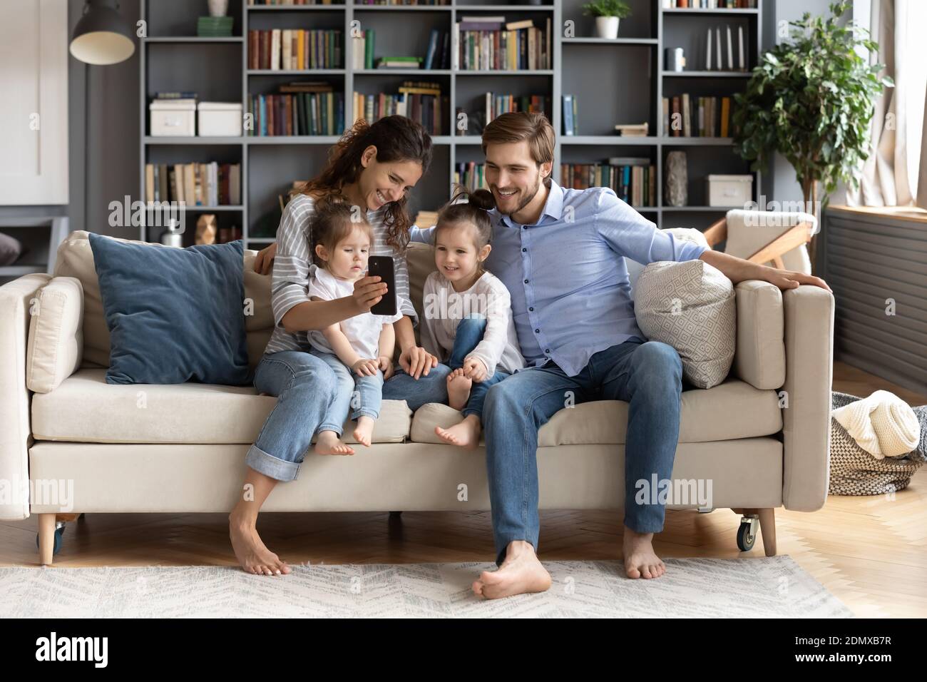 Happy parents relax at home using smartphone with small children Stock ...