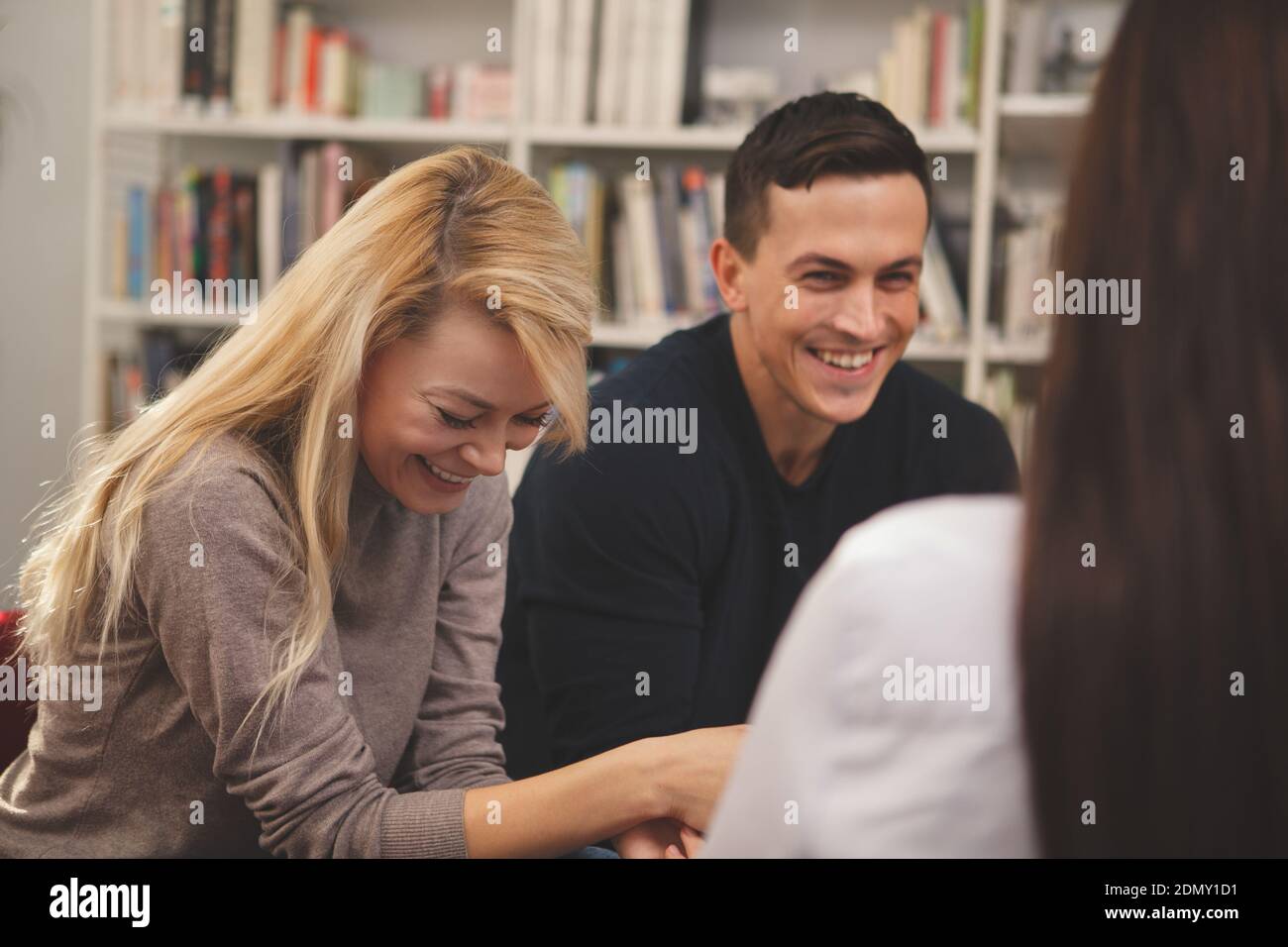 Happy college friends laughing joyfully, talking at the campus library ...