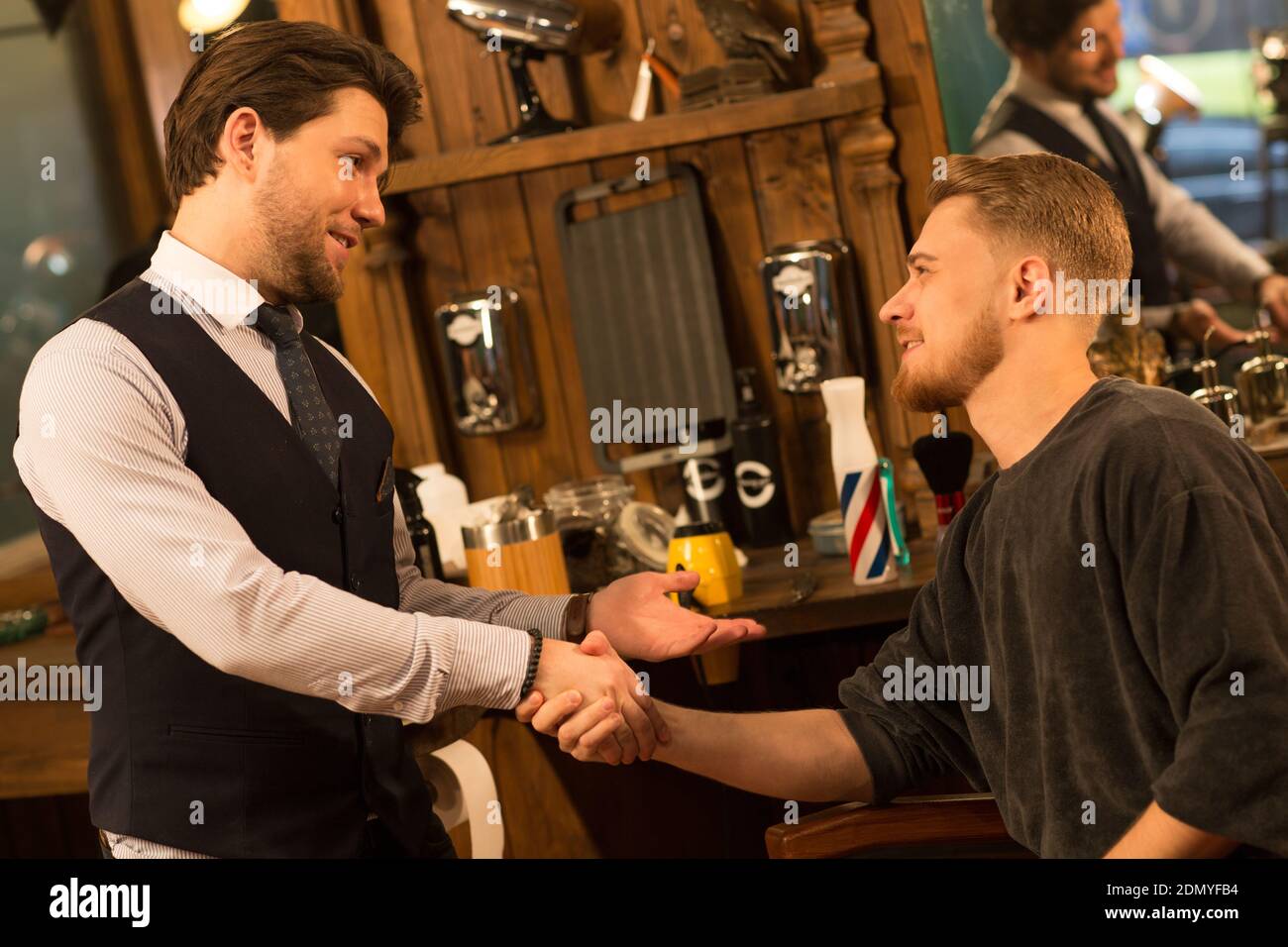 Professional barber shaking hands with his happy male client after ...