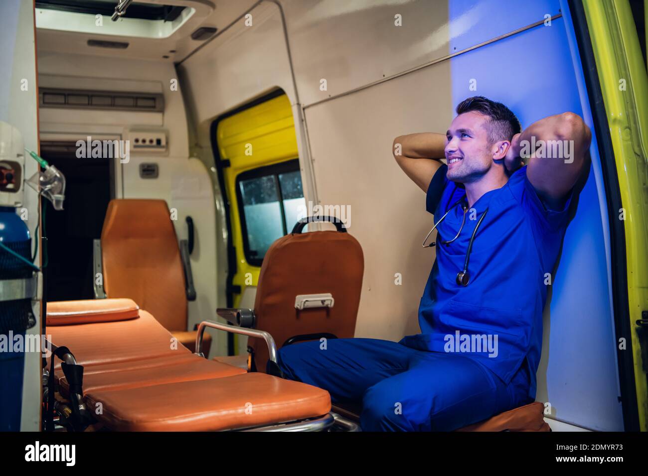 A dreamy medical worker sitting in an ambulance car with a mild smile ...