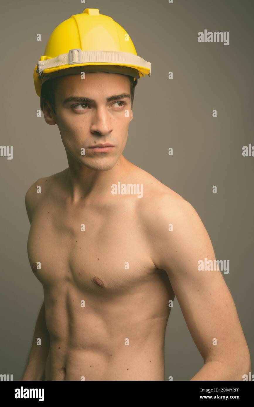 Young handsome man construction worker shirtless against gray ...