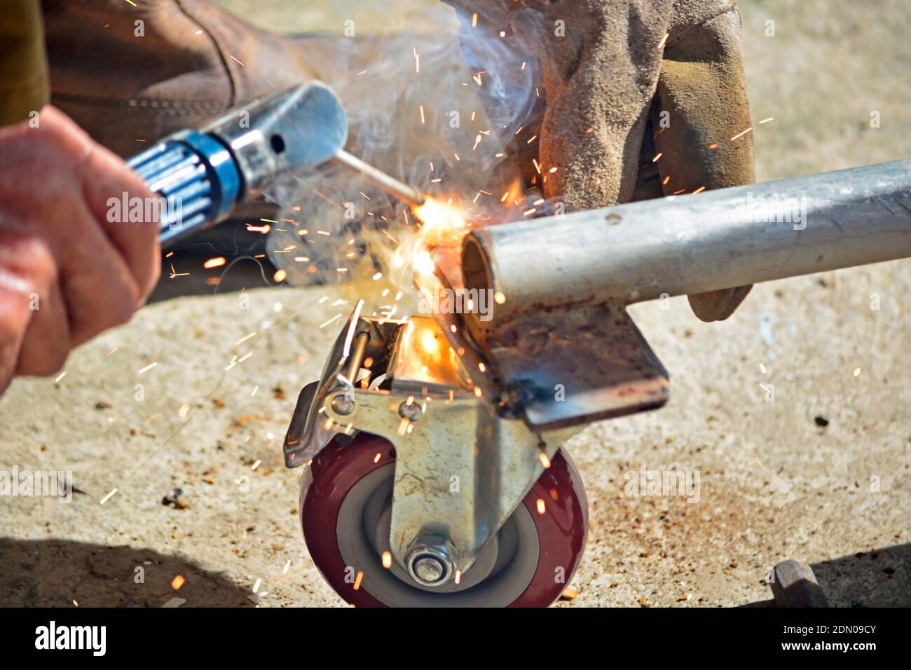 Worker with a welding machine fixing a caster wheels with fiery sparks ...