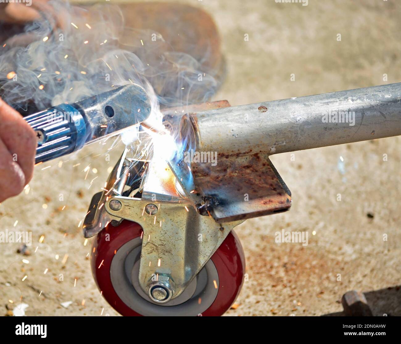 Worker with a welding machine fixing a caster wheels with fiery sparks ...
